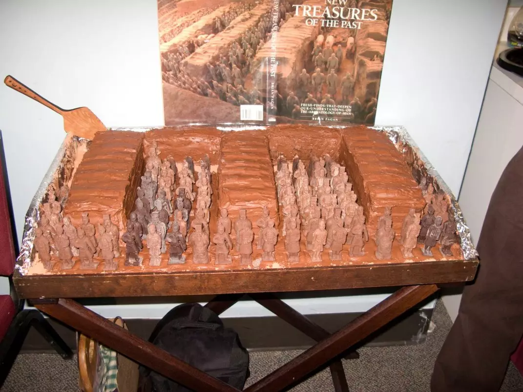 Smeđa, čokoladna torta rekreacija kineske grobnice sa smeđom, čokoladnom rekreacijom ratnika od terakote unutra. Torta je izložena na smeđom drvenom poslužavniku.