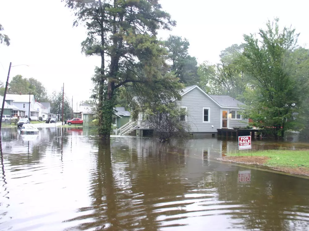 Billede af et oversvømmet kvarter i North Carolina. Gaden er oversvømmet med vand, og en bil sidder halvvejs fast i den. Vandet kommer op til husenes verandaer. EN