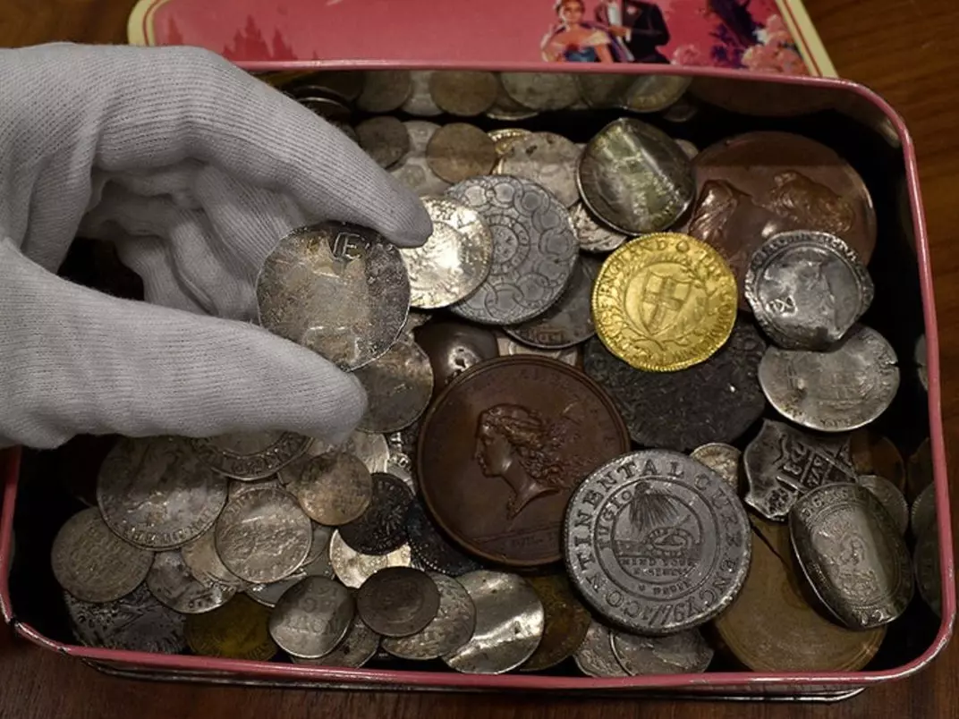 Novčić Nove Engleske držan je iznad lima s raznim starim novčićima