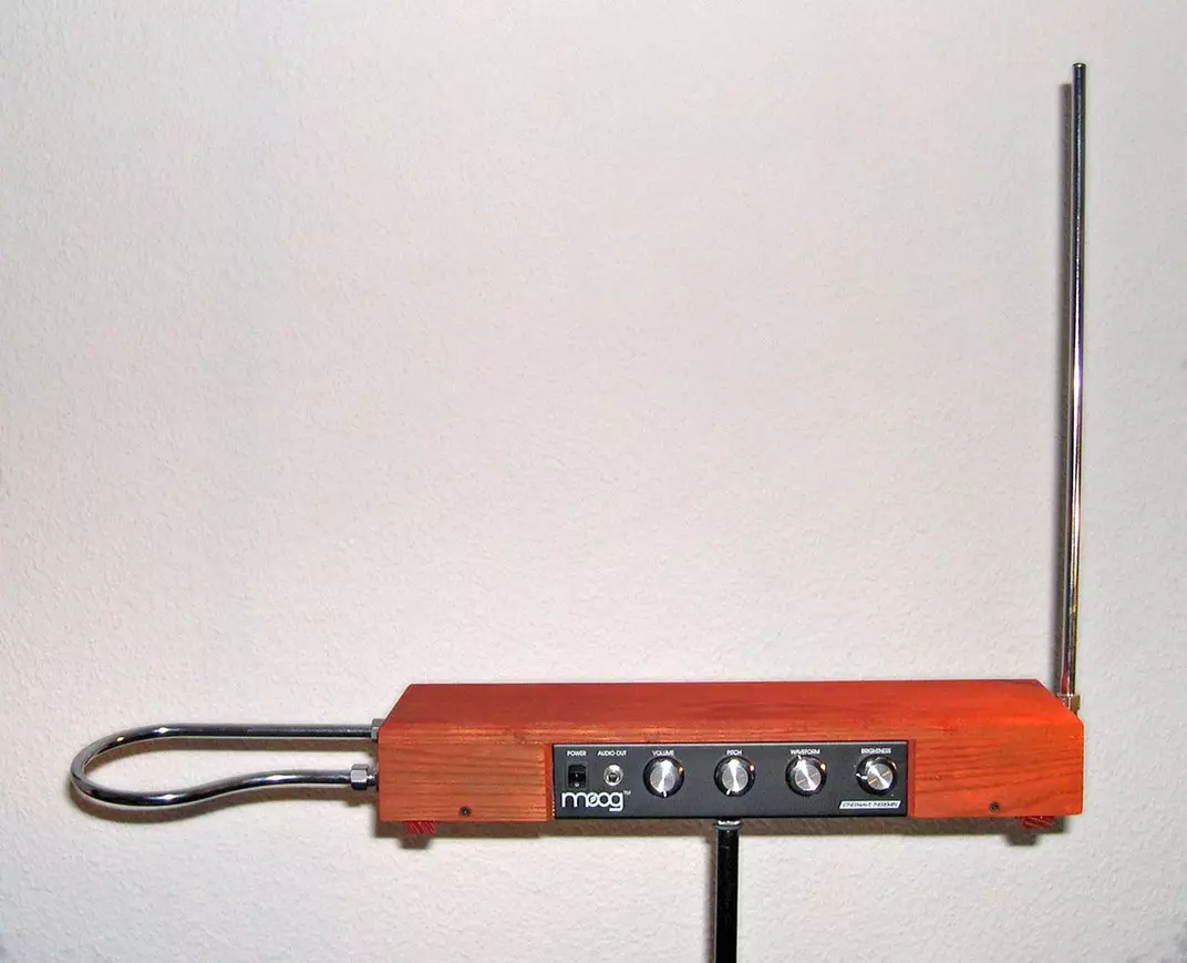 一个带有按钮的橙色盒子，类似于收音机，有一个金属环突出在它的一侧（我们的左边）和一个长金属杆以直角竖立在另一侧，就像一个收音机天线（我们的右边）
