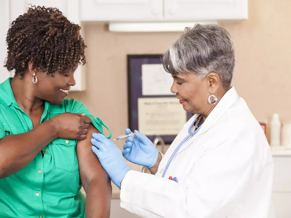 Une image d'une femme de couleur recevant un vaccin d'un médecin. Le médecin est une femme de couleur vêtue d'une blouse blanche.