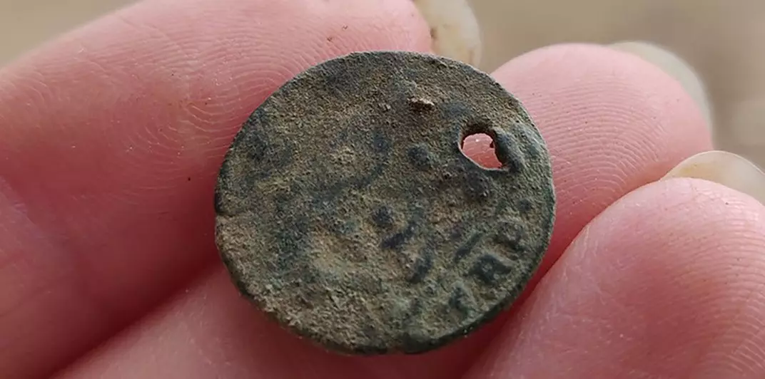 रोमन साम्राज्य के छेद के साथ जंग लगे गंदे सिक्के को हाथ में पकड़े हुए तस्वीर
