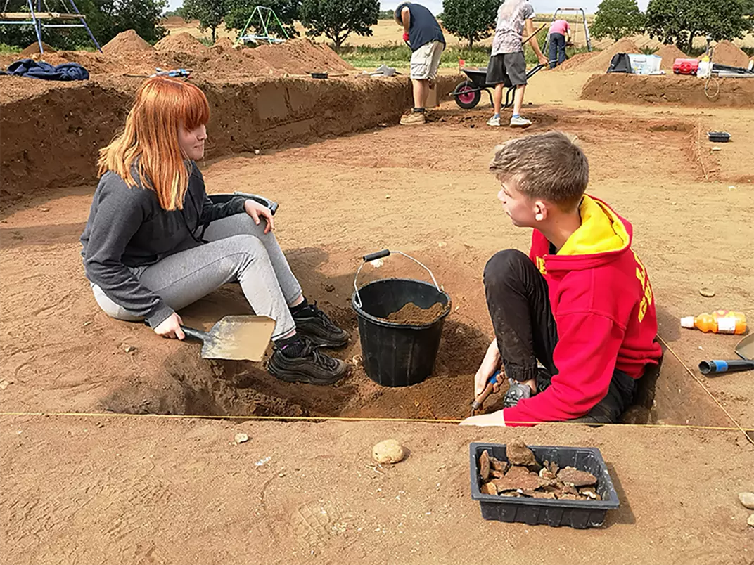 En ung dreng og kvinde sidder ved hul med gravematerialer