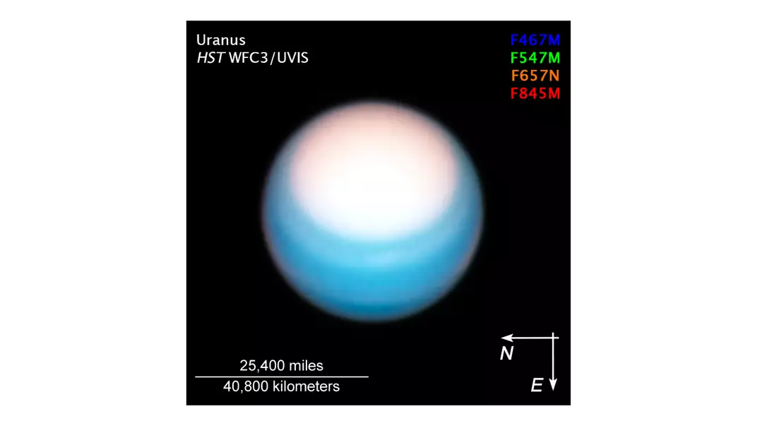 Een afbeelding van uranus badend in ultraviolet licht. De planeet ziet er blauw uit met een grote witte vlek in de richting van het noordelijk halfrond