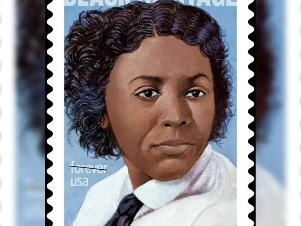 Một con tem có chân dung của Edmonia Lewis, một người phụ nữ Da đen với mái tóc gợn sóng cắt xén trong áo sơ mi trắng và cà vạt đen, trên nền xanh lam