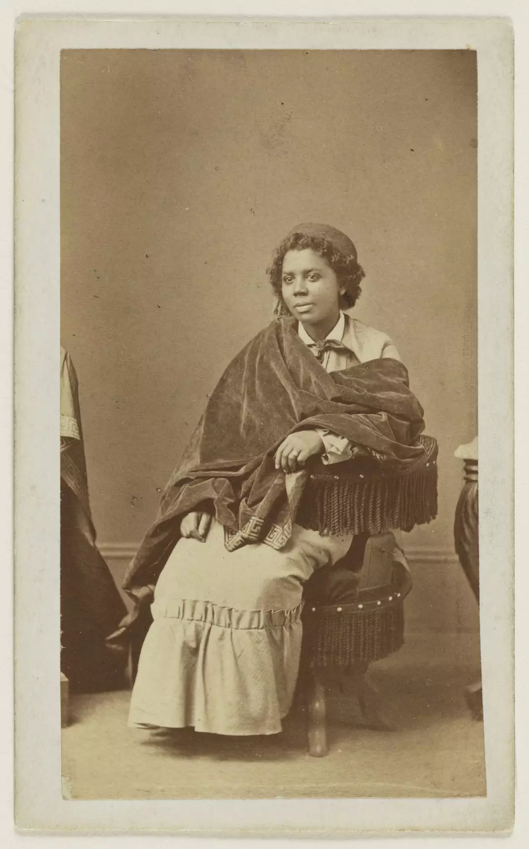 Edmonia Lewis, juodaodė garbanotais plaukais su skara ir suknele, sėdi ir žiūri į tolį sepijos atspalvio portretu.