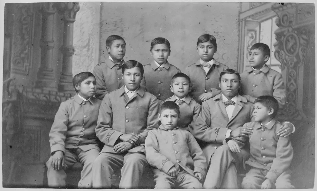 Sekelompok anak laki-laki, beberapa remaja dan beberapa sangat muda, dalam pakaian resmi gaya militer, berpose di depan latar belakang hiasan