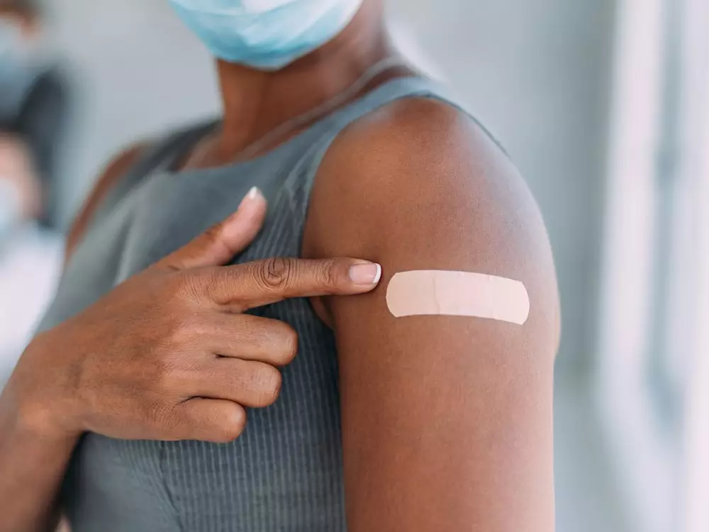 Juoda moteris po vakcinacijos rodo į ranką su tvarsčiu