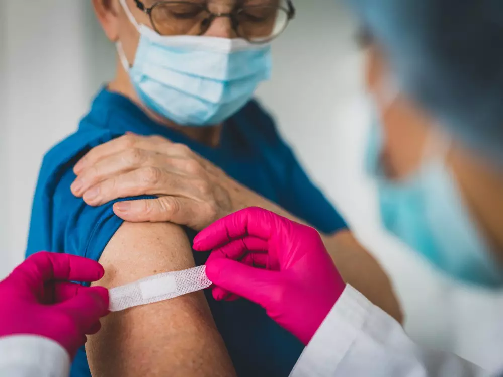Een dokter met roze handschoenen brengt een pleister aan op de arm van een oudere vrouw