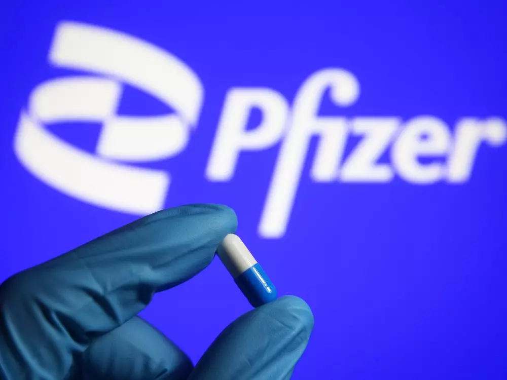 يد مرتدية القفاز تحمل قرصًا أمام شعار شركة Pfizer