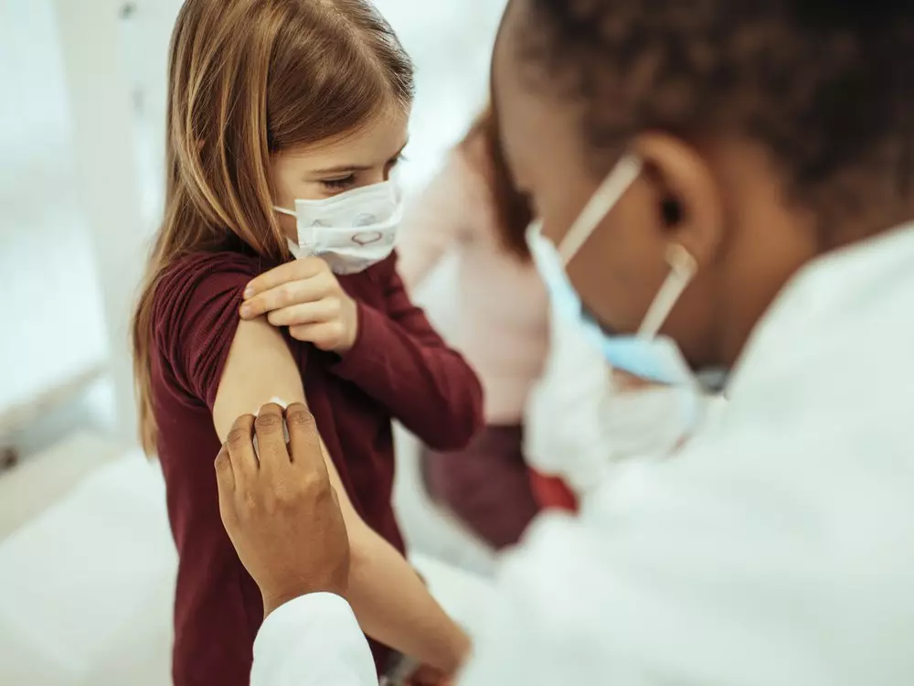 Một nữ bác sĩ đeo mặt nạ tiêm phòng cho một cô gái trẻ đeo mặt nạ
