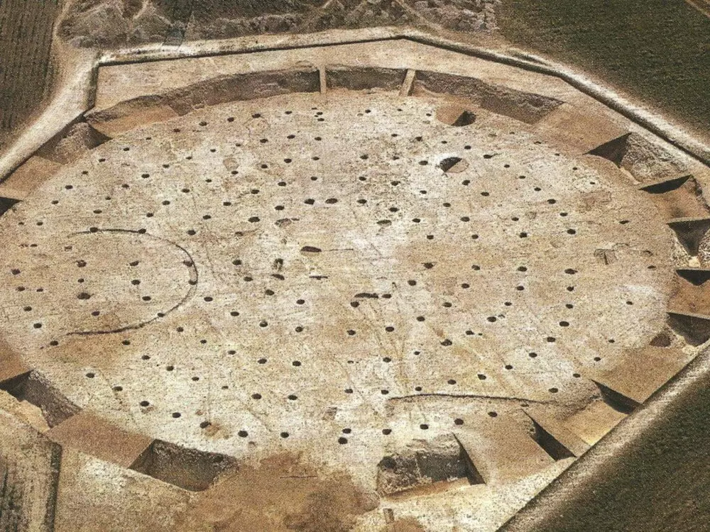Uma vista aérea de terra arenosa com vários buracos em círculos concêntricos e uma vala ao redor de toda a formação