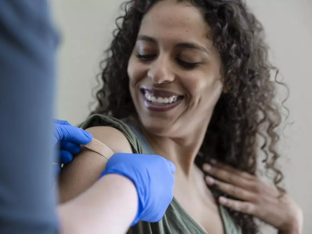 팔에 반창고를 붙이고 의사로부터 백신을 맞는 흑인 여성의 사진