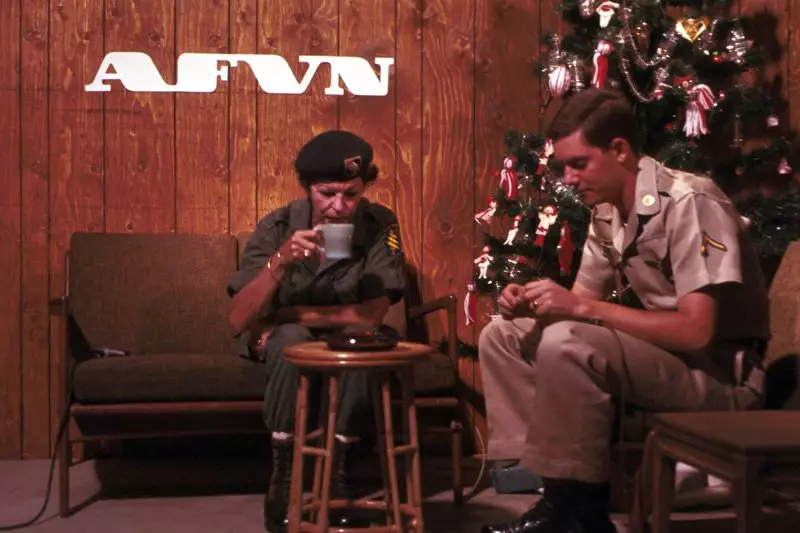 Martha Raye interviu Dick Ellis. Rėjus ir Elis sėdi ant kėdžių šalia papuoštos Kalėdų eglutės medinėmis dailylentėmis išklotame kambaryje.