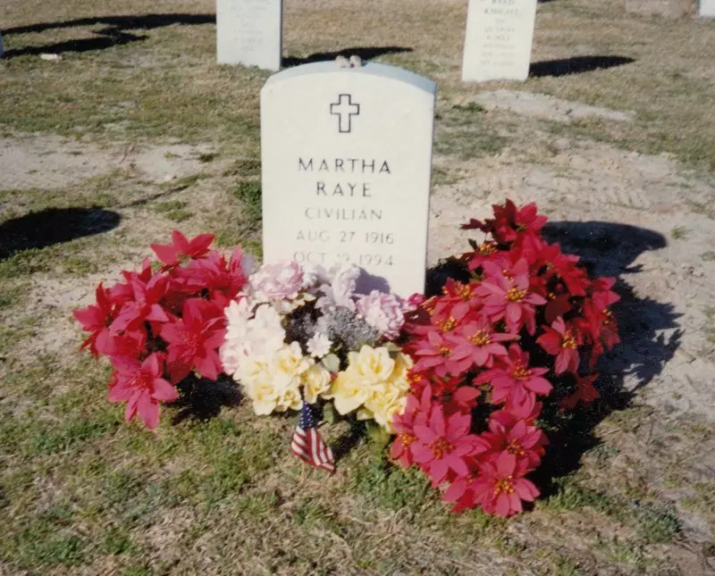 Martha Raye se grafsteen versier met blomme en 'n klein Amerikaanse vlag. Ander grafstene in die Fort Bragg Main Post-begraafplaas is in die agtergrond sigbaar.