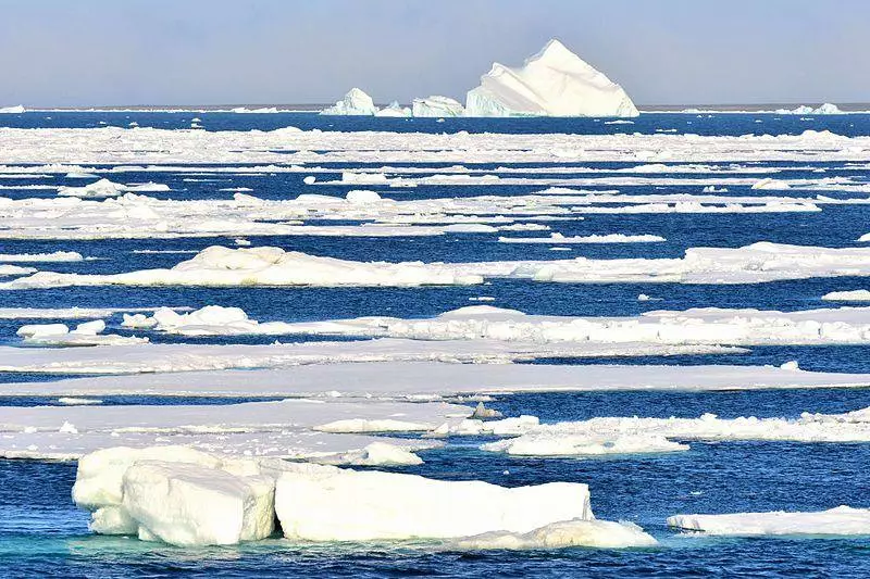 Eng Seelandschaftsfoto vum Laptev Mier am Polarkrees. Am Virdergrond schwiewen kleng Äisplacken op hellblo Waasser. Et gëtt eng méi grouss Äisplack laanscht den Horizont, wou den Ozean de groen Himmel bedeit.