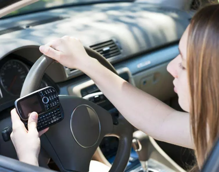 Një adoleshente i dërgon mesazhe celularit teksa drejton makinën.