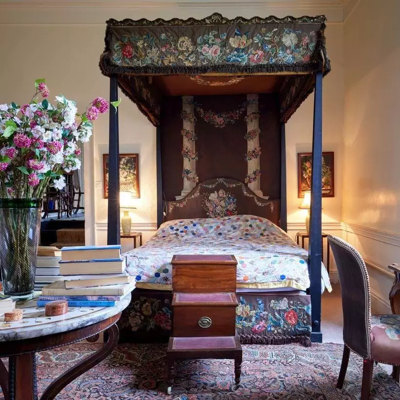 Un llit ornamentat de quatre cantonades amb un edredó de colors i envoltat de penjades brodades amb motius florals