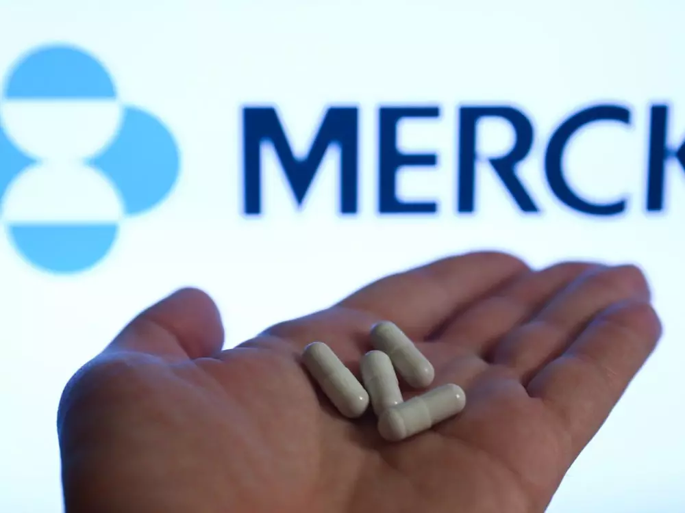 Merck 브랜드 배경에 대해 4개의 흰색 캡슐을 들고 있는 왼손의 이미지