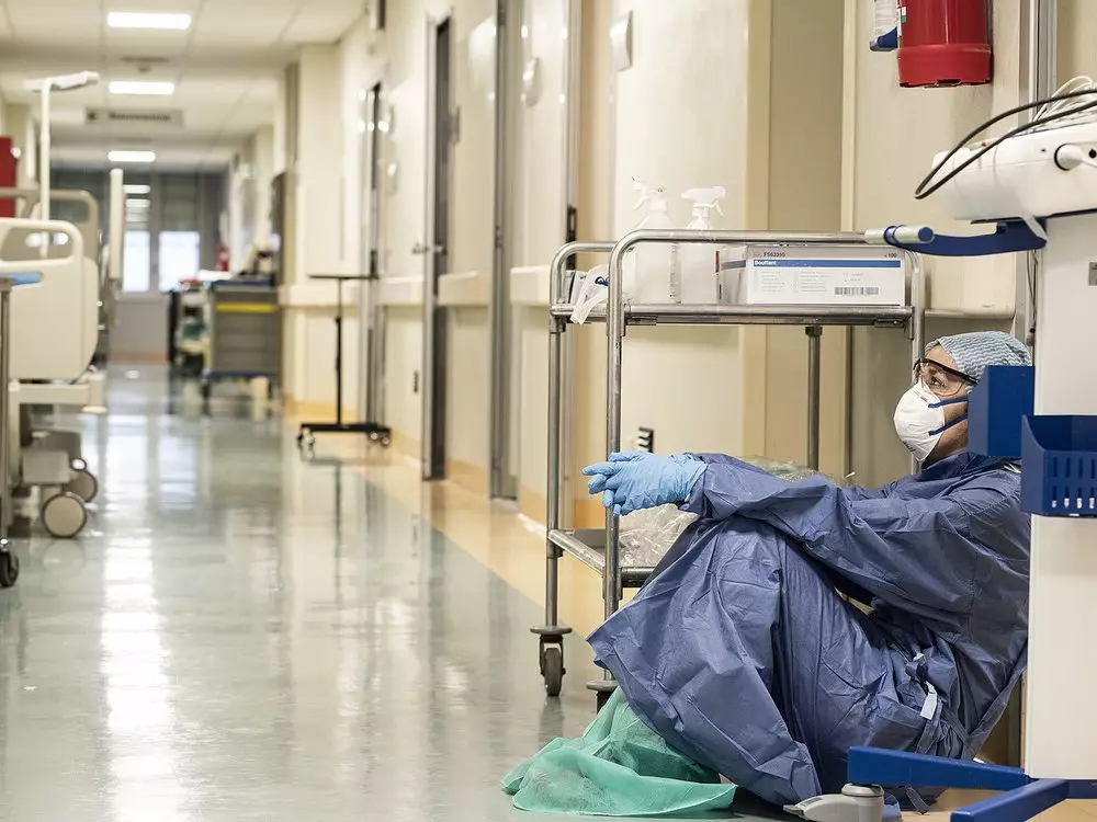 Eine Ärztin mit Schutzausrüstung sitzt auf dem Boden eines Krankenhausflurs in Italien