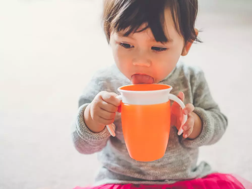 Vaikas, laikantis oranžinį puodelį