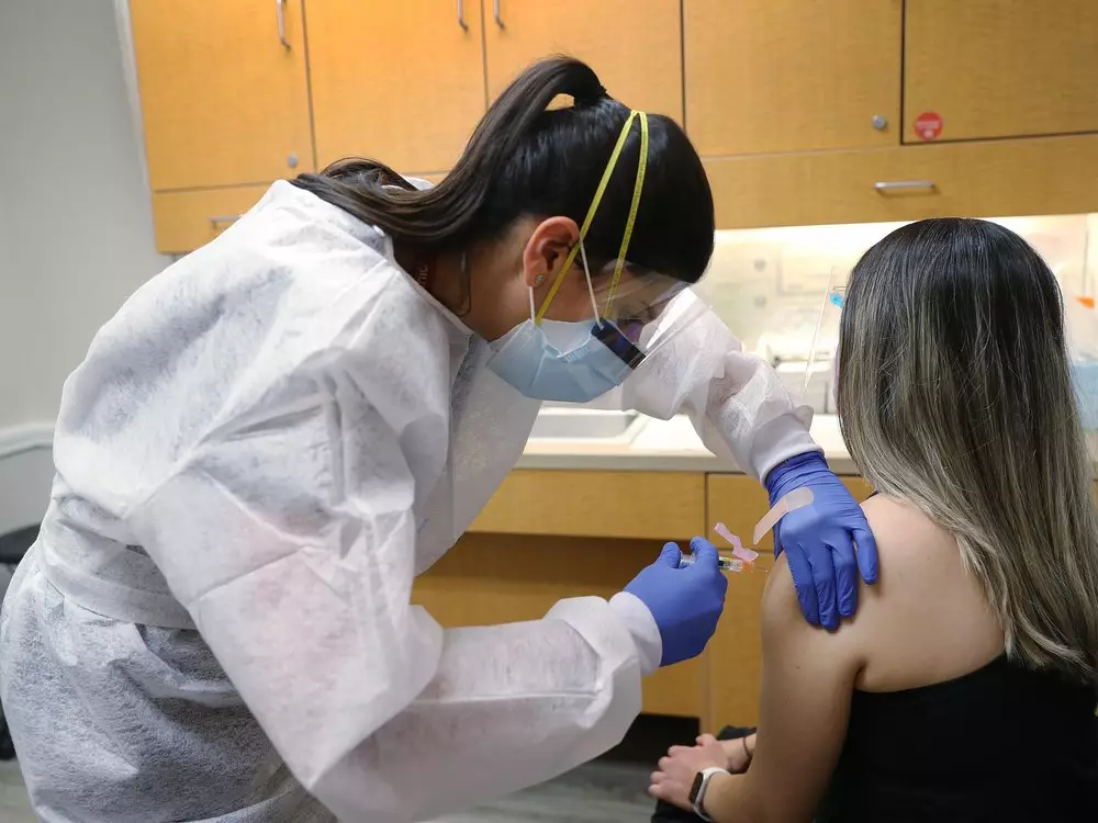 Una enfermera practicante usa equipo de protección personal mientras administra una vacuna contra la influenza a un paciente