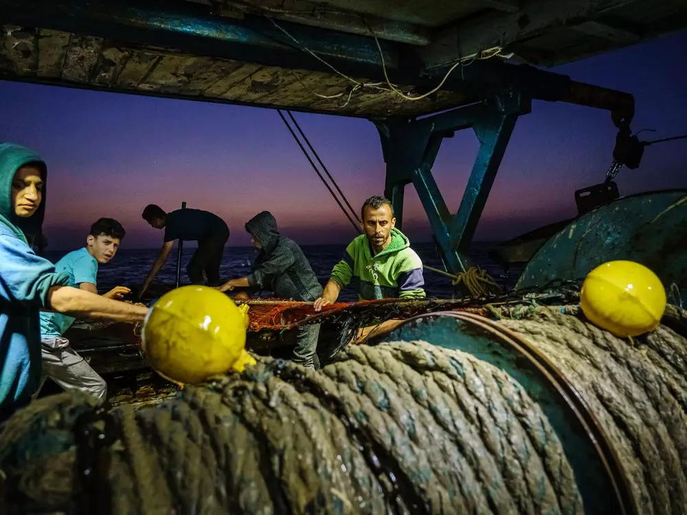 A halászok alkonyatkor kézzel húzzák a kötelet egy halászhajón Gázában