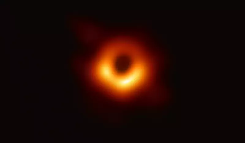 Ada titik hitam di tengah foto. Itu dikelilingi oleh cincin oranye terang yang paling terang di bagian bawah lingkaran. Sisa foto adalah latar belakang semua hitam.