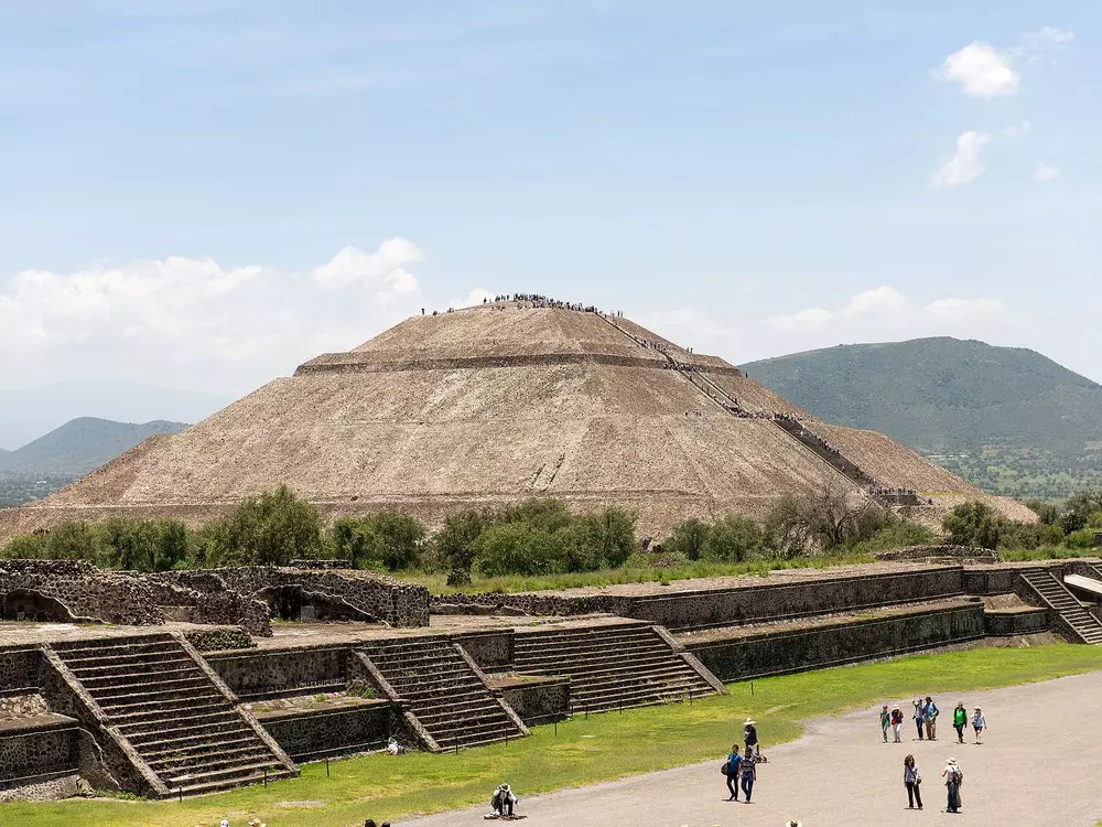 A view of the Pyramid of the Sun at Teotihuacan, a huge pyramid that stands several stories tall over an expansive avenue populated by tourists
