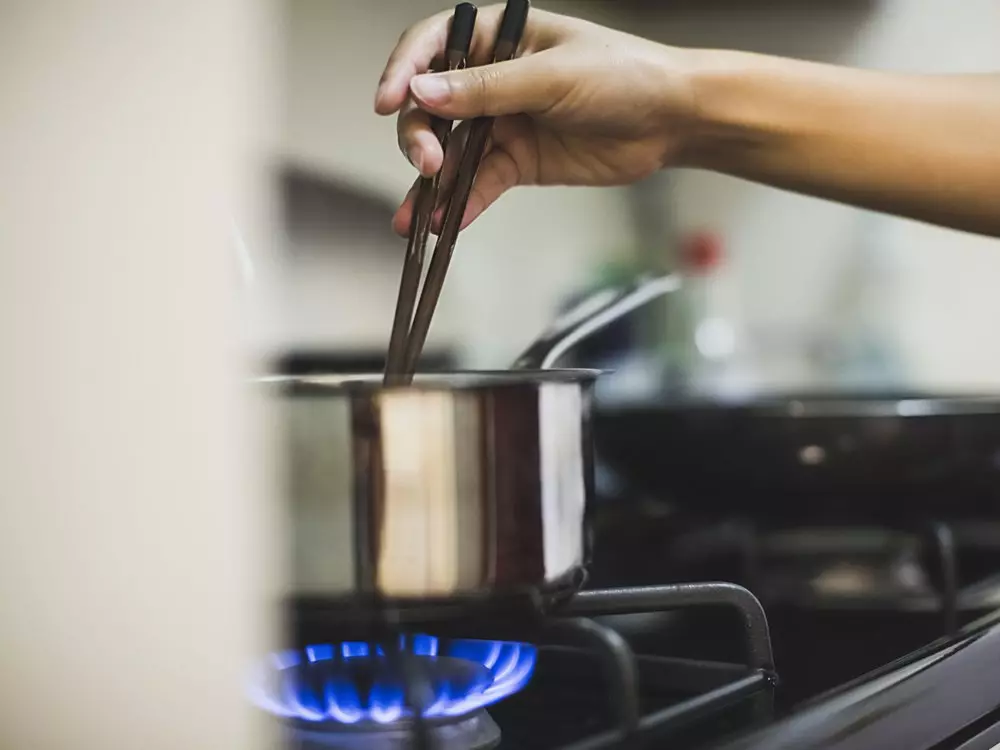 Kobieca ręka mieszająca garnek pałeczkami nad zapaloną kuchenką gazową
