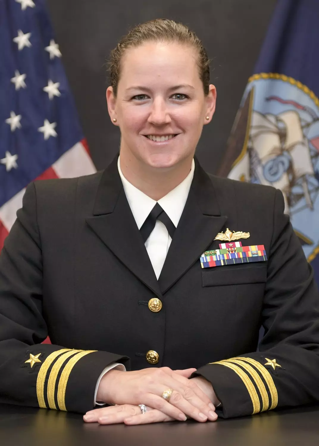 زن جوان با لباس نیروی دریایی مشکی که در مقابل پرچم ایالات متحده لبخند می زند