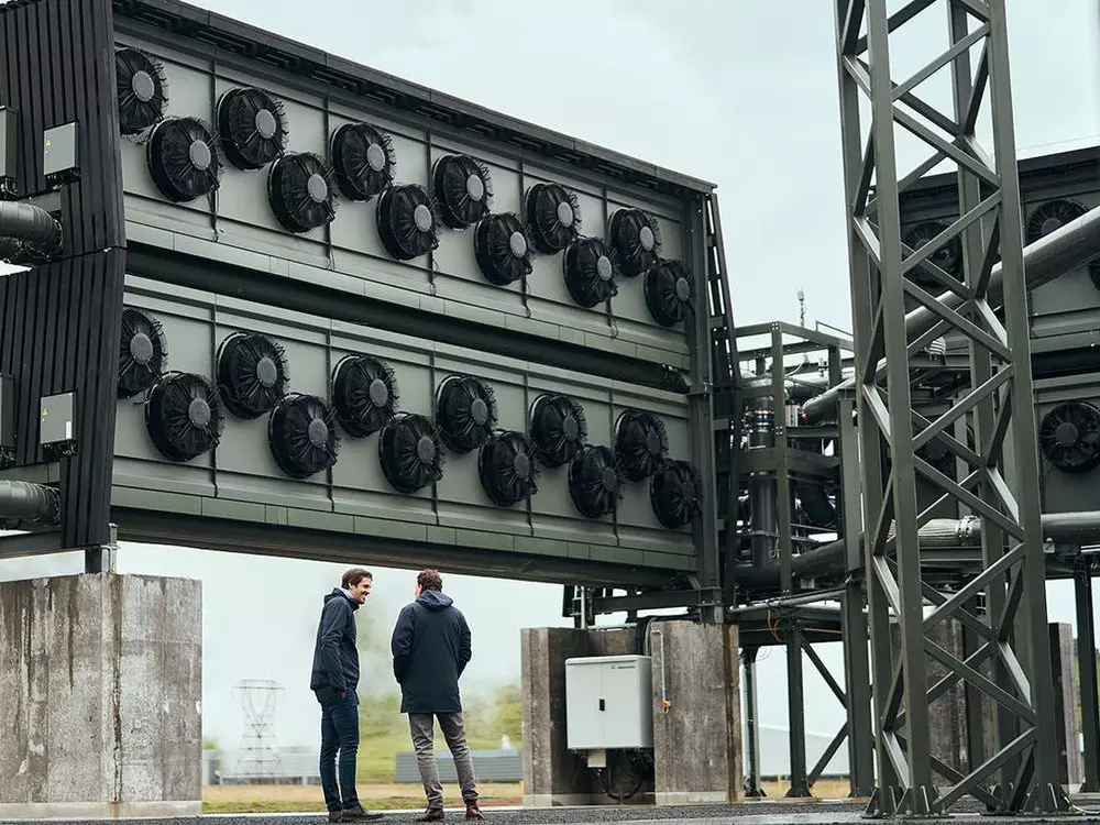 Dua pria berdiri di depan dinding tinggi kipas angin di fasilitas penangkap karbon Orca di Islandia