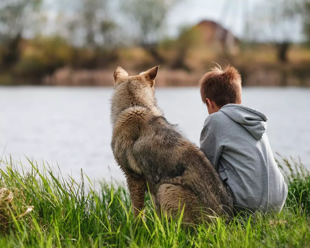 Un niño y un perro se sientan junto a un cuerpo de agua.