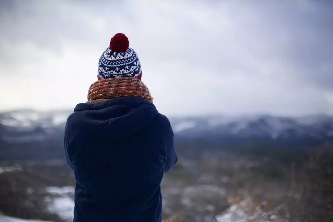 Osoba koja nosi pleteni šešir i šal stoji na litici.