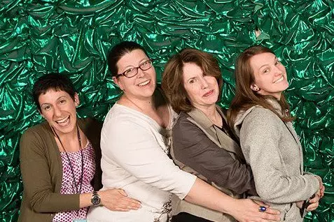 Quatro mulheres caucasianas posam para uma foto em frente a um pano de fundo verde