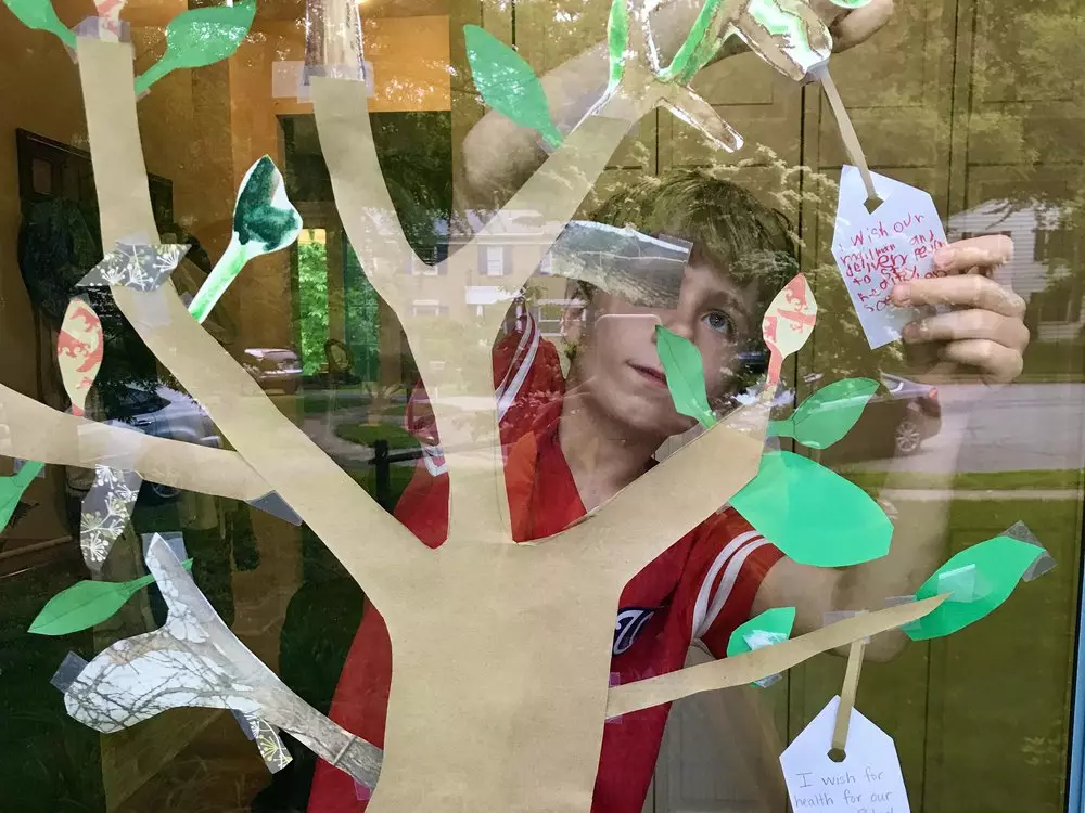 En gutt legger til et ønske om helsen til leveringsarbeidere under 2020-pandemien. Dette papirønsketreet er inspirert av kunstneren Yoko Onos Wish Tree for Washington, som vises i Hirshhorn Museums skulpturhage.