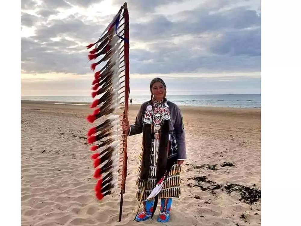 Command Sergeant Major Julia Kelly (U.S. Army retired), one of 80 Native American delegates to the 75th anniversary observance of D-Day, stands on Omaha Beach. Kelly holds an eagle feather staff, an American Indian symbol of respect, honor, and patriotism. (Courtesy of Julia Kelly)