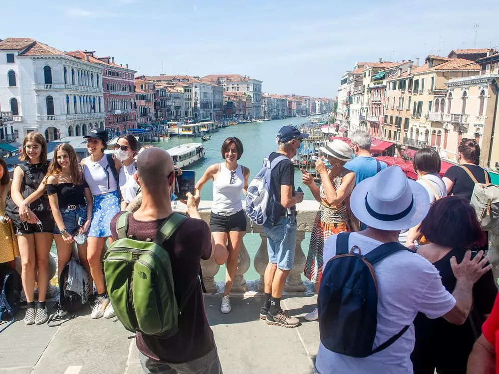 En grupp turister står och poserar för foton framför en venetiansk kanal, några bär masker och andra inte