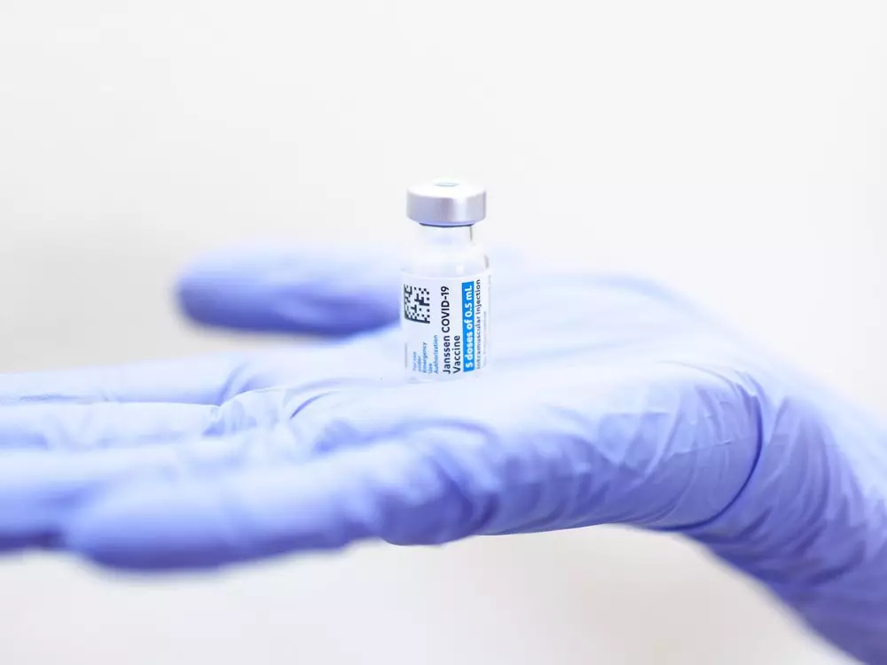 La mano guantata blu tiene una piccola fiala di vetro del vaccino covid-19 Johnson e Johnson