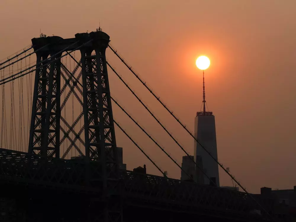 Ang araw ay lumulubog sa likod ng Manhattan Bridge at One World Trade Center sa isang manipis na ulap na likha ng usok