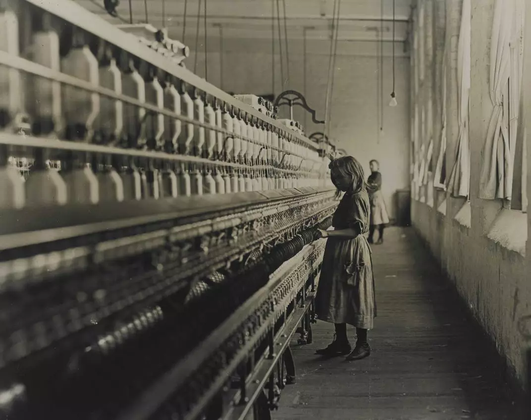 Mustavalkoinen valokuva nuoresta tytöstä mekossa työskentelemässä tekstiilitehtaalla
