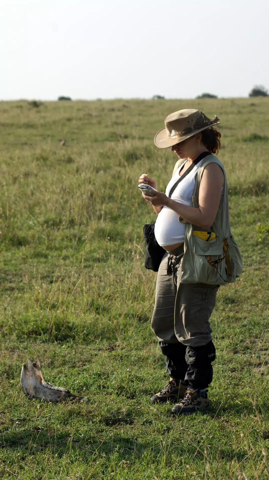 Briana Pobiner nangtung dina datar, kabuka, sawah héjo jukut di Kenya.