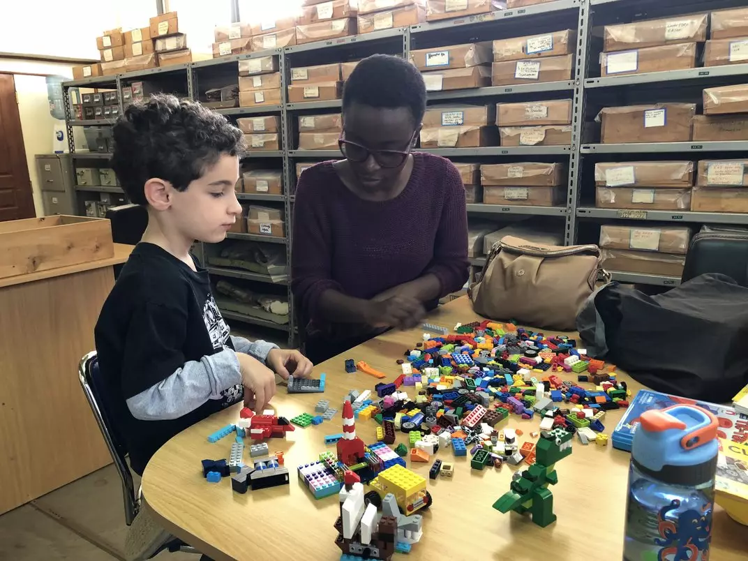 Ein kleiner Junge und eine erwachsene Frau an einem Holztisch spielen mit bunten Legos.