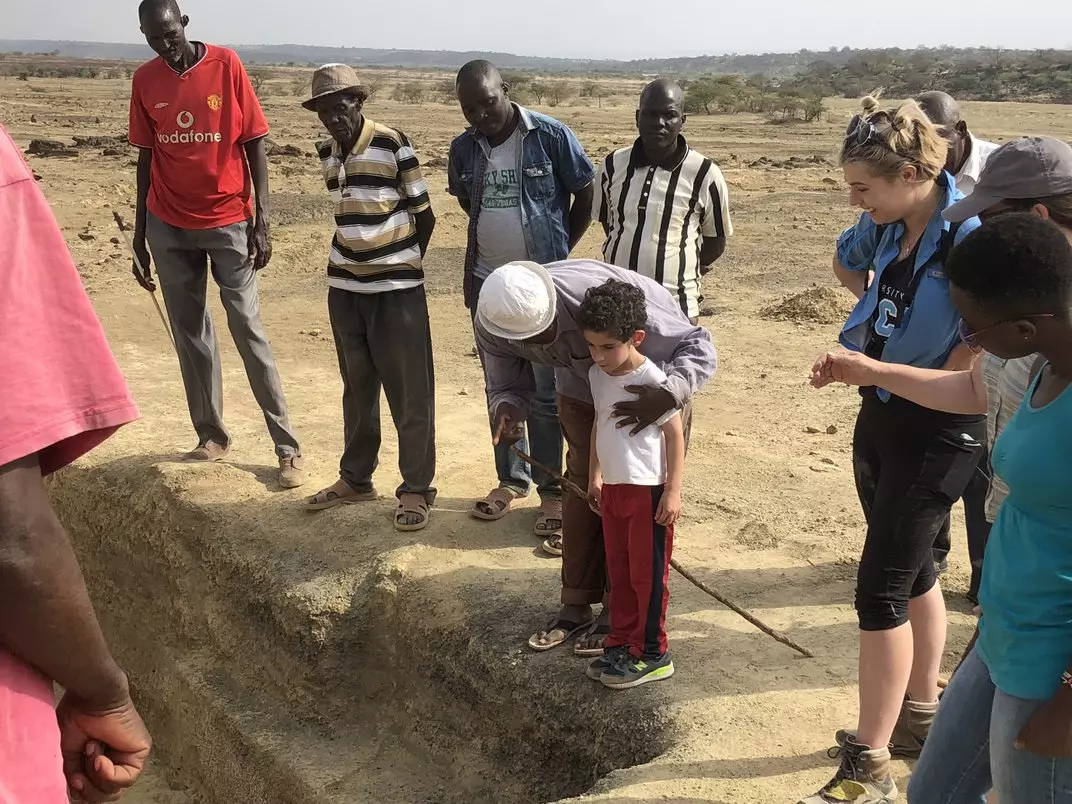 En ung dreng omgivet af en gruppe voksne i en tør, brun ørken i Kenya.