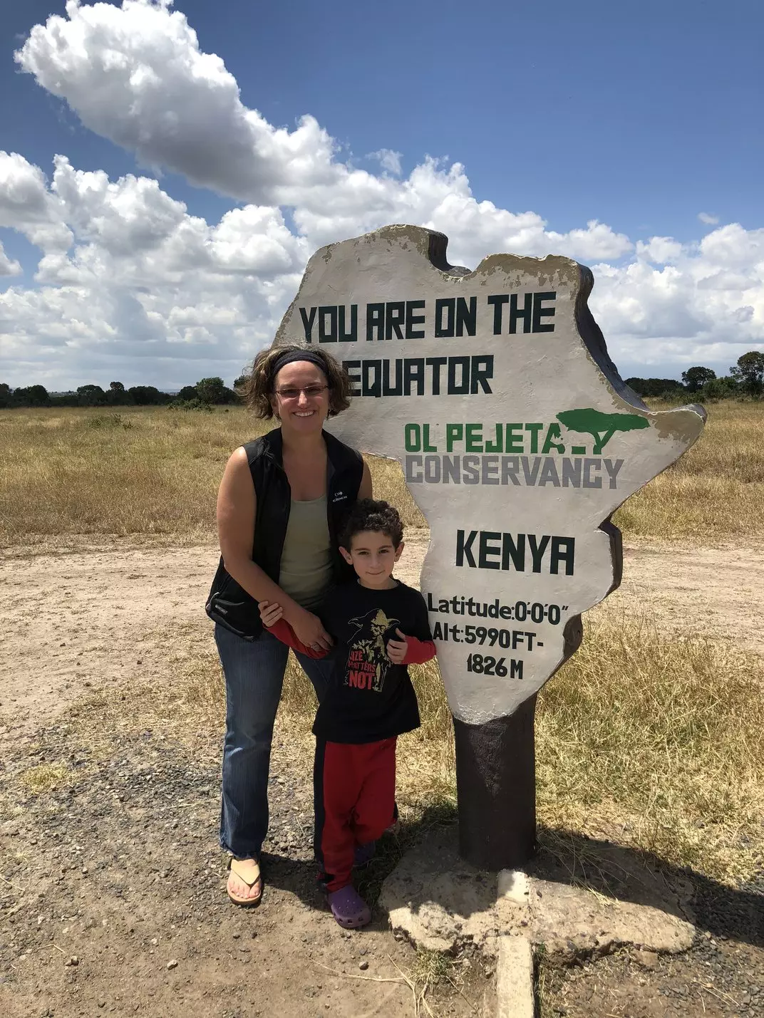 Ọdọmọkunrin ati obinrin agba kan lẹgbẹẹ ami funfun ti o n samisi equator ni Kenya.