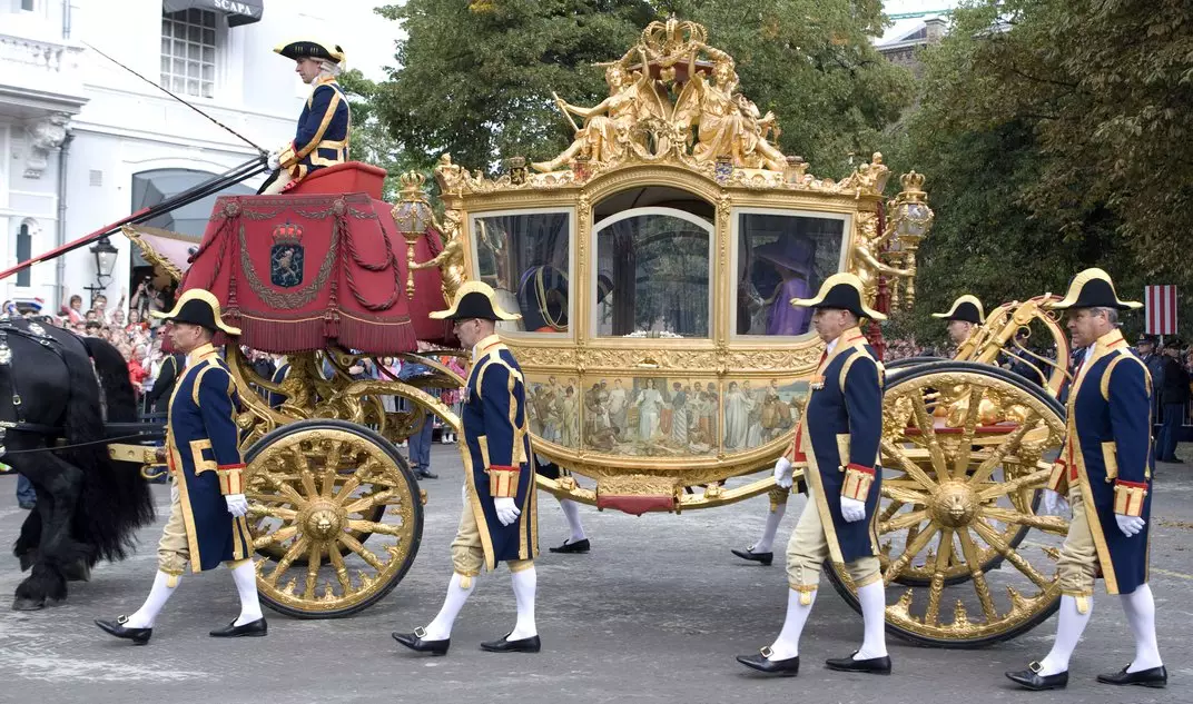 Мъже, облечени в кралски дрехи, вървят до изискана карета, позлатена в злато с големи колела. Отстрани на каретата, триптих изобразява бяла жена на трон, която получава подаръци от полуголи черни хора, които се покланят или гледат надолу