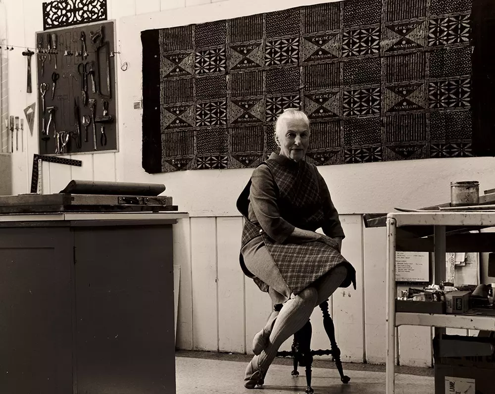 Photograph of Dorr Bothwell photographed in her studio surrounded by tools and textiles.