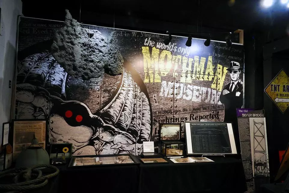 Ipakita sa sulod sa usa ka museyo nga adunay itom nga mga bungbong ug mga lamesa nga puno sa mga karatula, mga litrato, ug usa ka pisi. Ang backdrop mabasa: “The world's only Mothman Museum” nga adunay cartoon nga mga ilustrasyon sa usa ka Mothman nga pula ang mga mata ug usa ka detective.