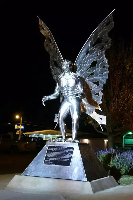 La stessa statua dell'Uomo Falena di notte, che brilla sotto un riflettore.