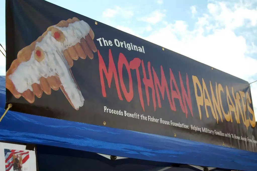 'n Reklamebord adverteer "The Original Mothman Pancakes," met 'n pannekoek in die vorm van 'n T, bedek met wit geklopte room, en twee rooi oë.